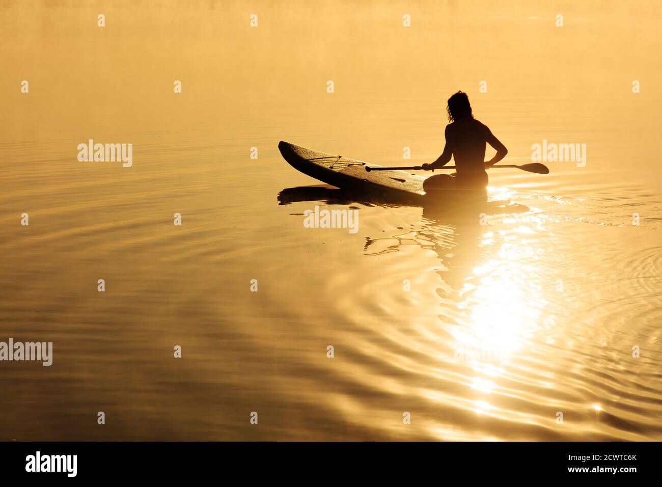 Man sitting on sup board and using paddle for swimming Stock Photo - Alamy