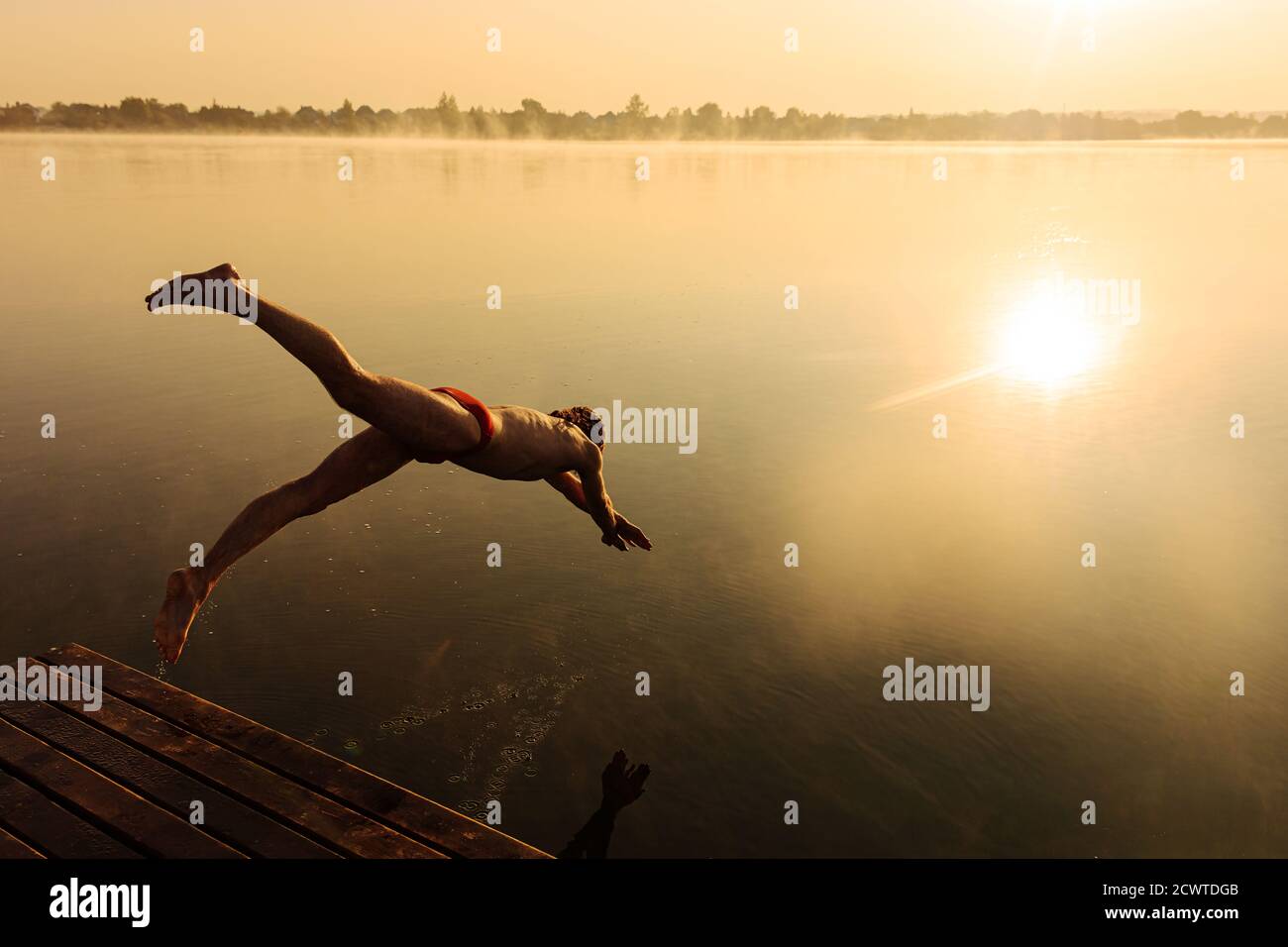 Active young man jumping into water from wooden pier Stock Photo - Alamy