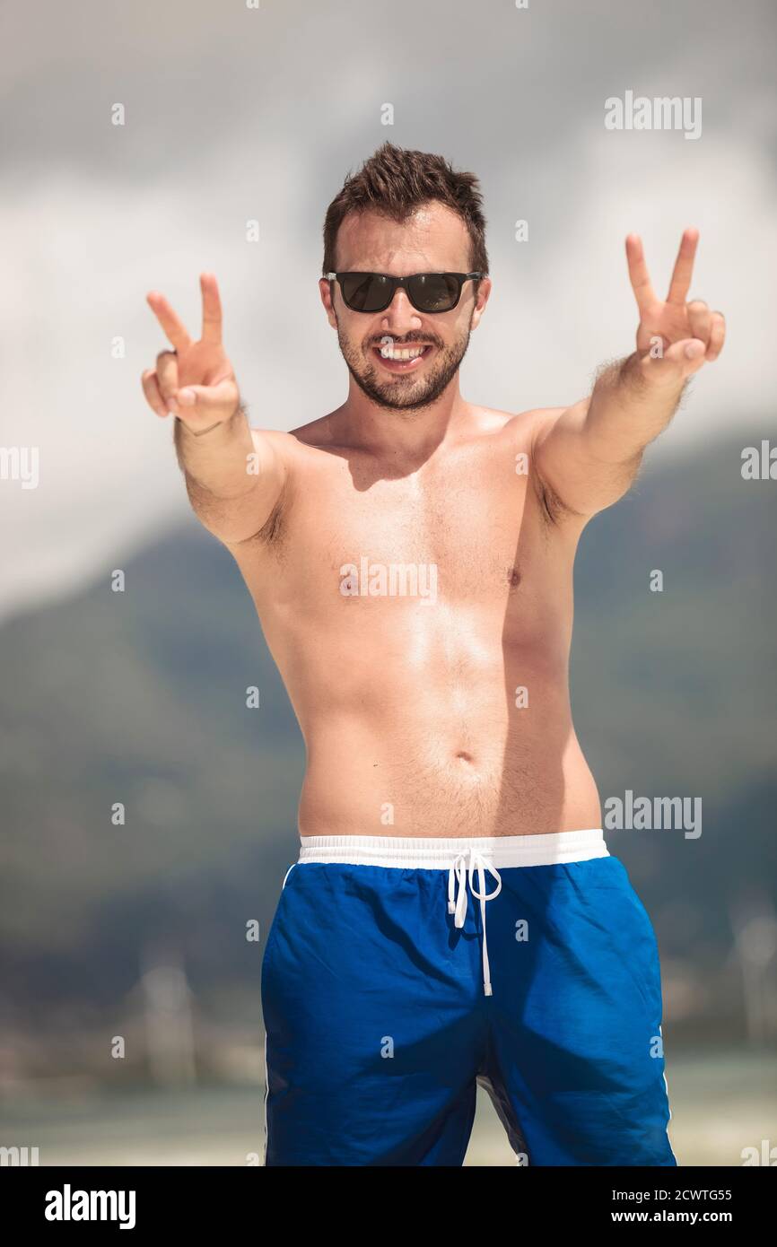 Portrait of a young happy man posing on the beach while showing the ...