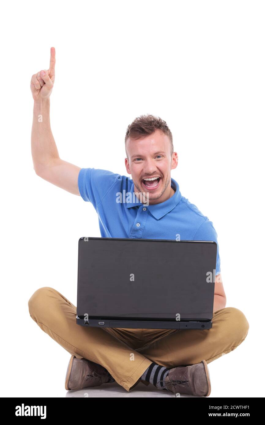 casual young man holding his laptop while sitting on the floor with his ...