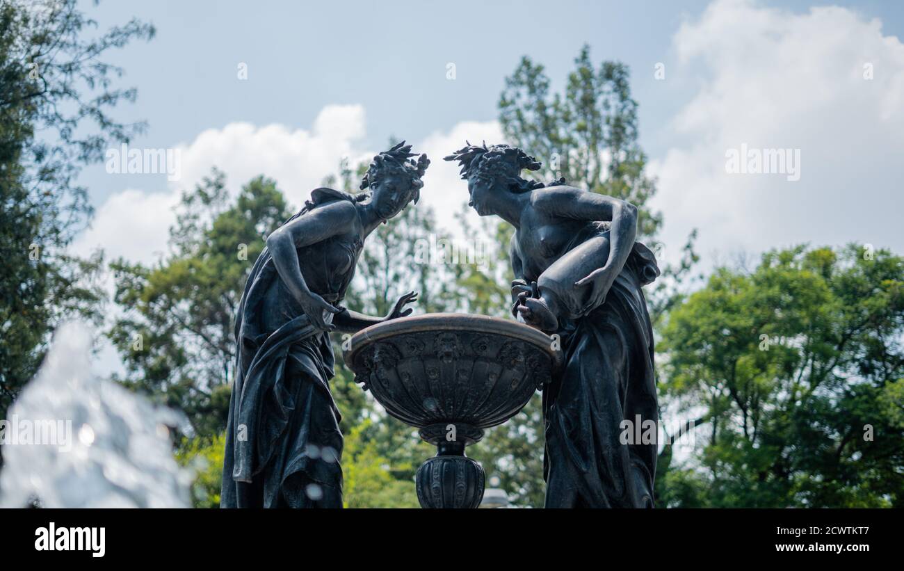 Bronze Statue of Two Women Pouring Down Water Into a Bird Waterer Stock ...
