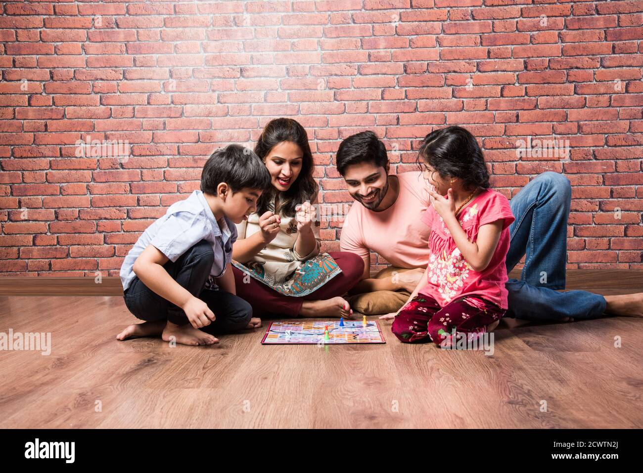 Indian young family of four playing board games like Chess, Ludo or ...