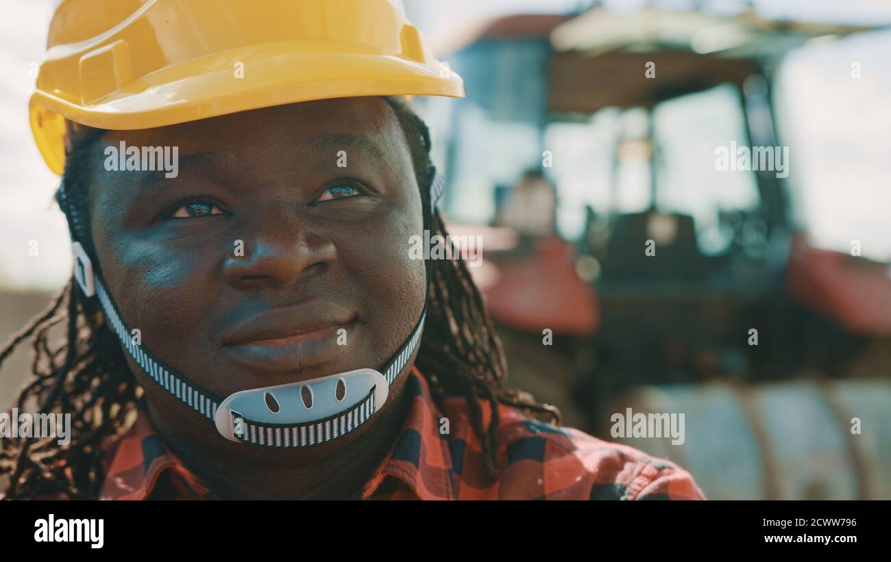 Portrait of african man with safety helmet on the farm. Tractor in the ...