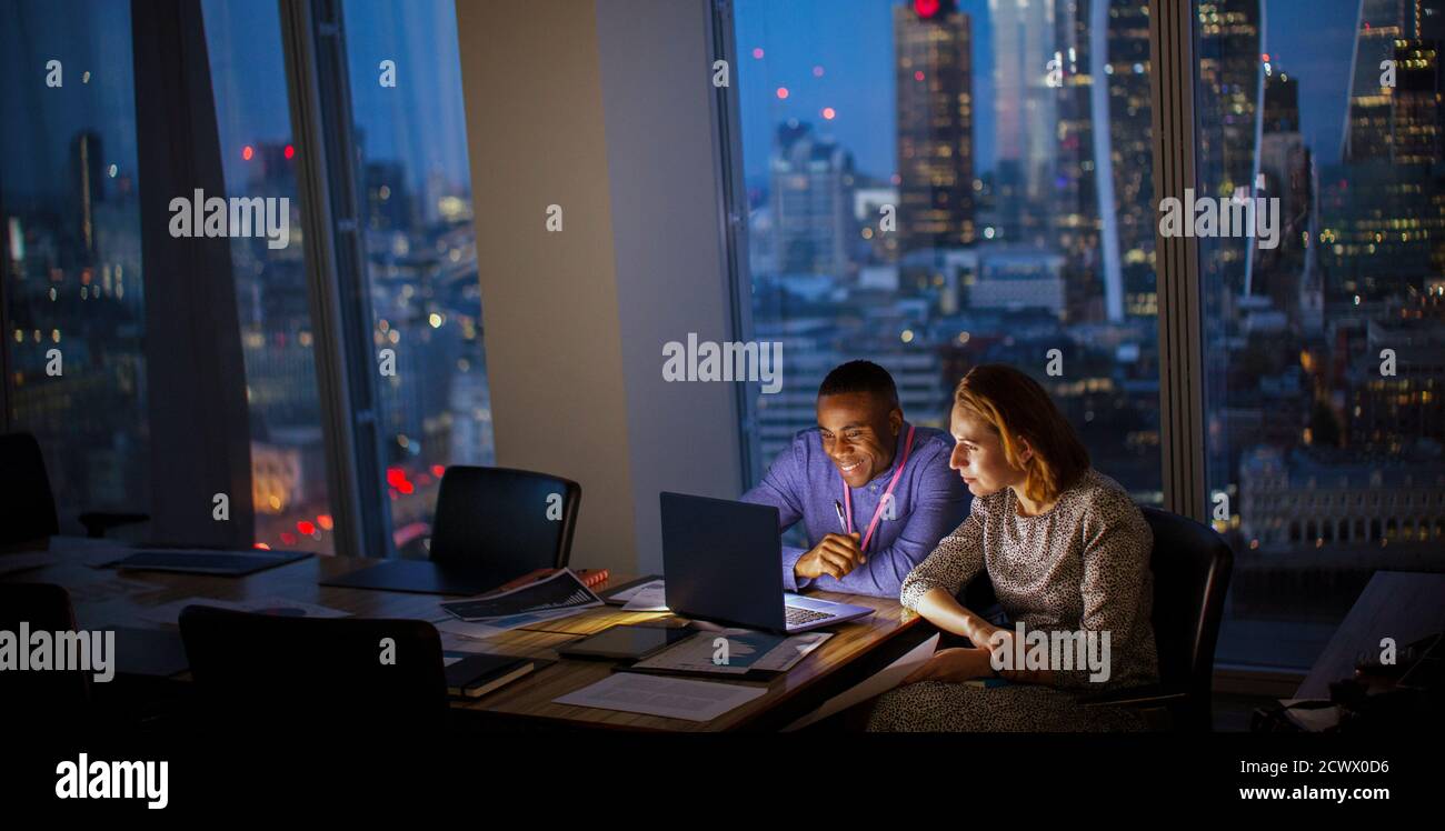 Business people working late at laptop in highrise office, London, UK ...
