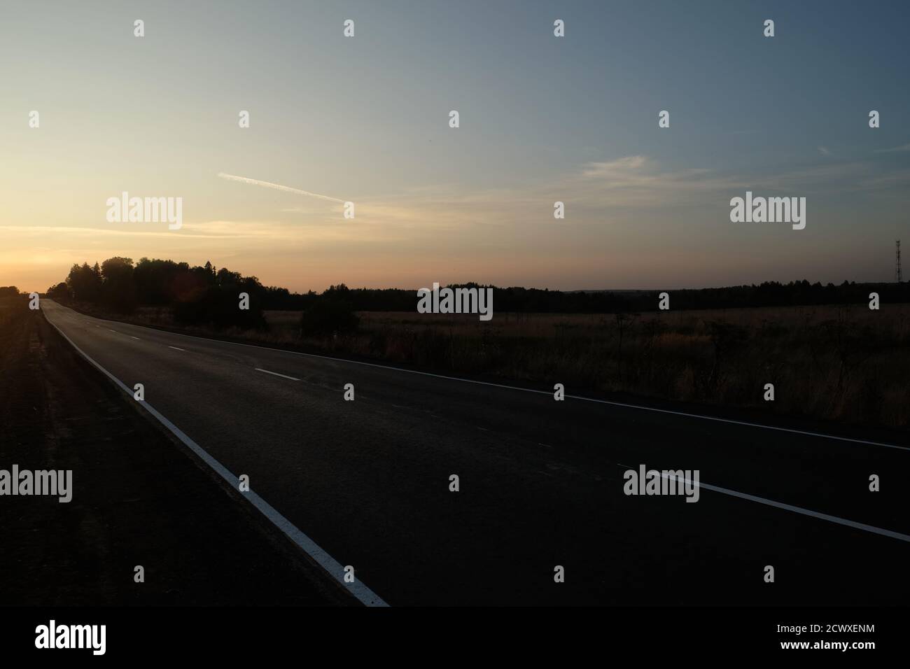 Direct empty suburban road with new road marking runs far to the horizon in the sunset in the ...