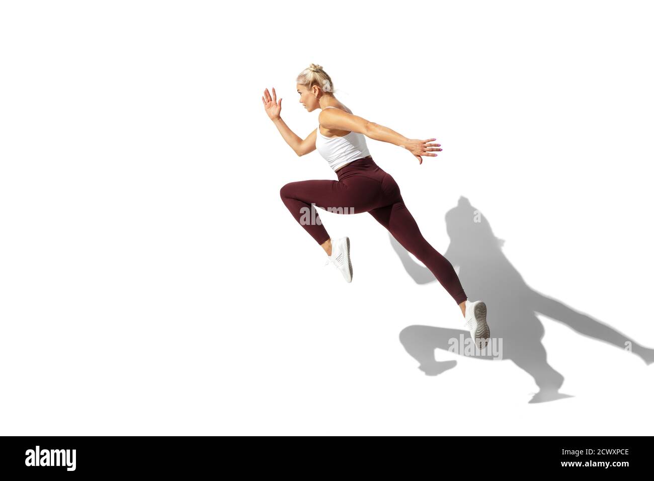 Running. Beautiful young female athlete practicing on white studio ...