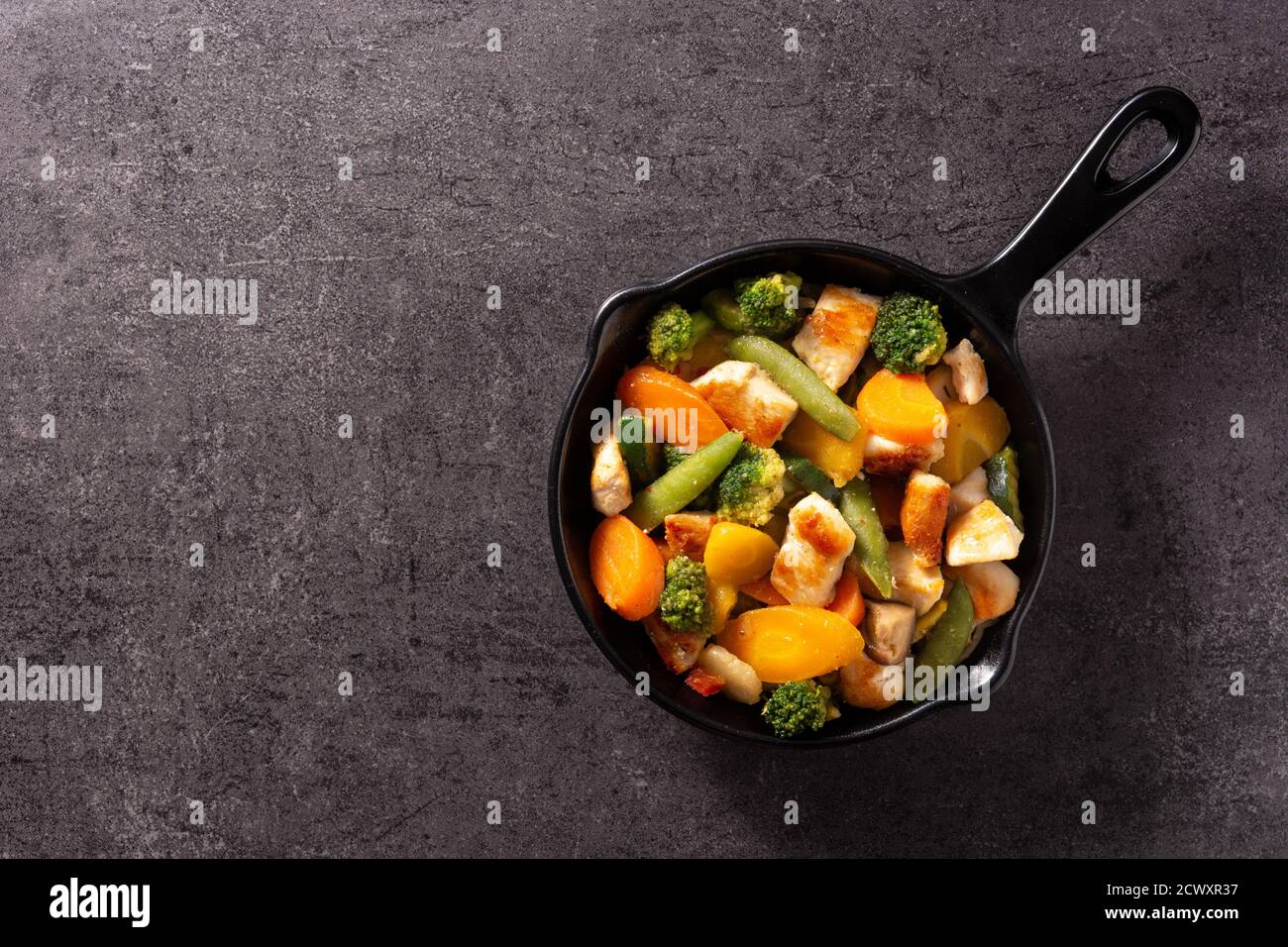 Stir fry chicken with vegetables on iron pan black background.Top view ...