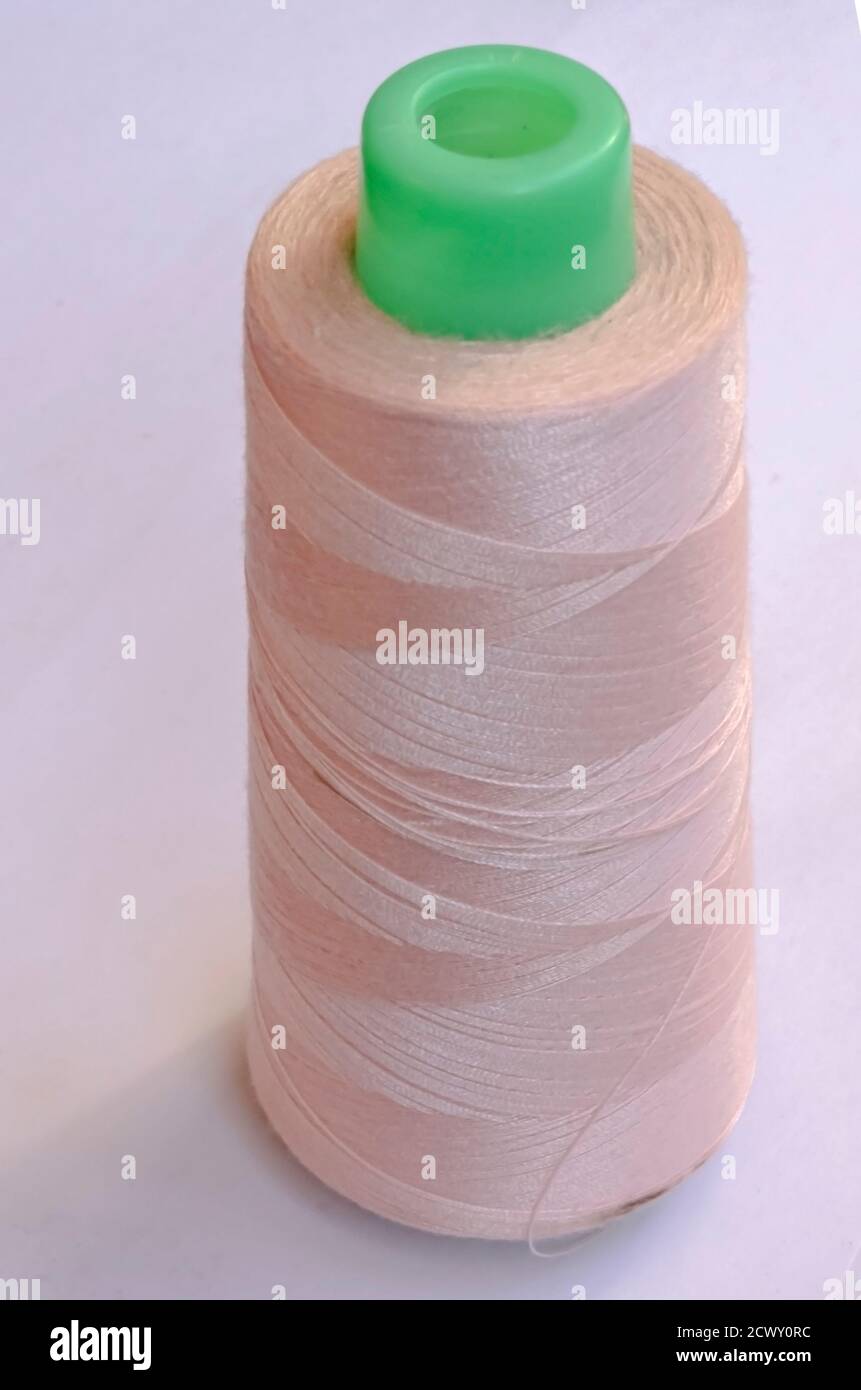A green cone spool with a hole in the center has on it pale pink thread ...