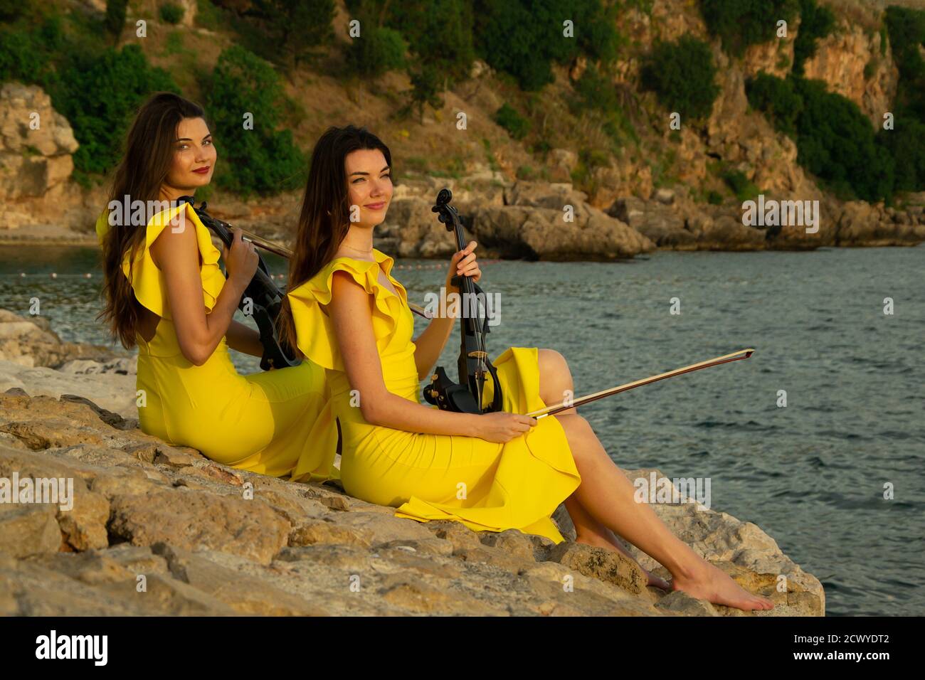 Two beautiful twin sisters violinists in yellow concert dresses are ...