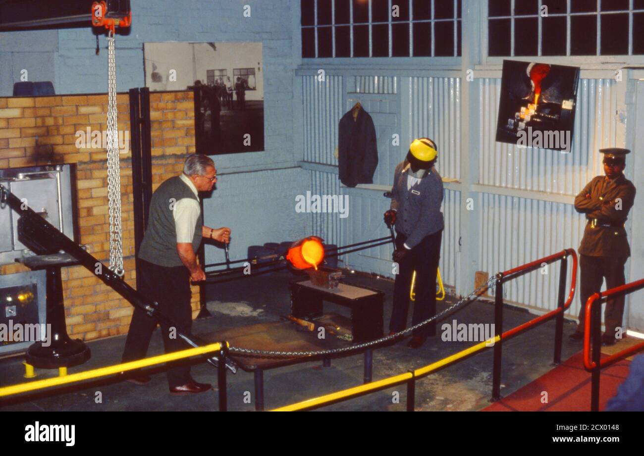 Two men pouring molten gold into a mould to make a bullion bar block ...