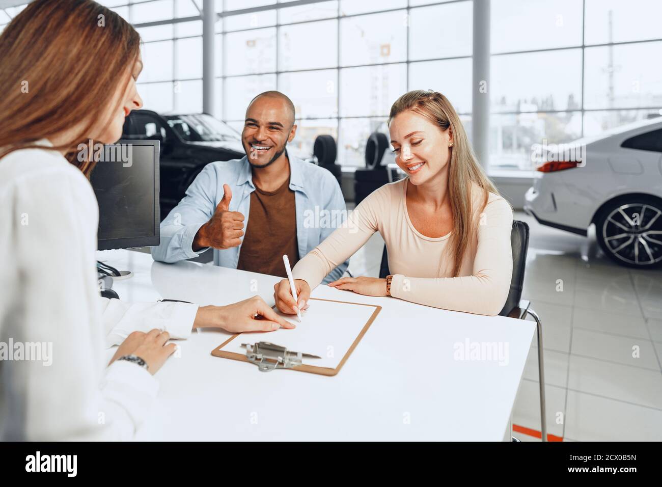 Beautiful young couple signs documents at car dealership showroom Stock ...