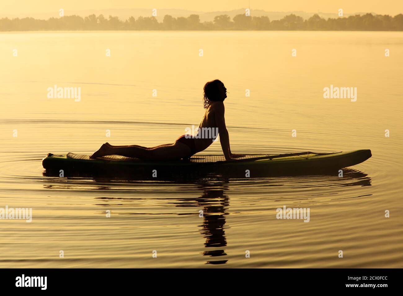 Active young guy in silhouette stretching body on sup board Stock Photo ...