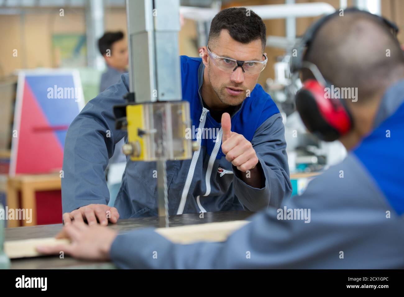 foreman giving thumbs up to carpenter using band saw Stock Photo - Alamy