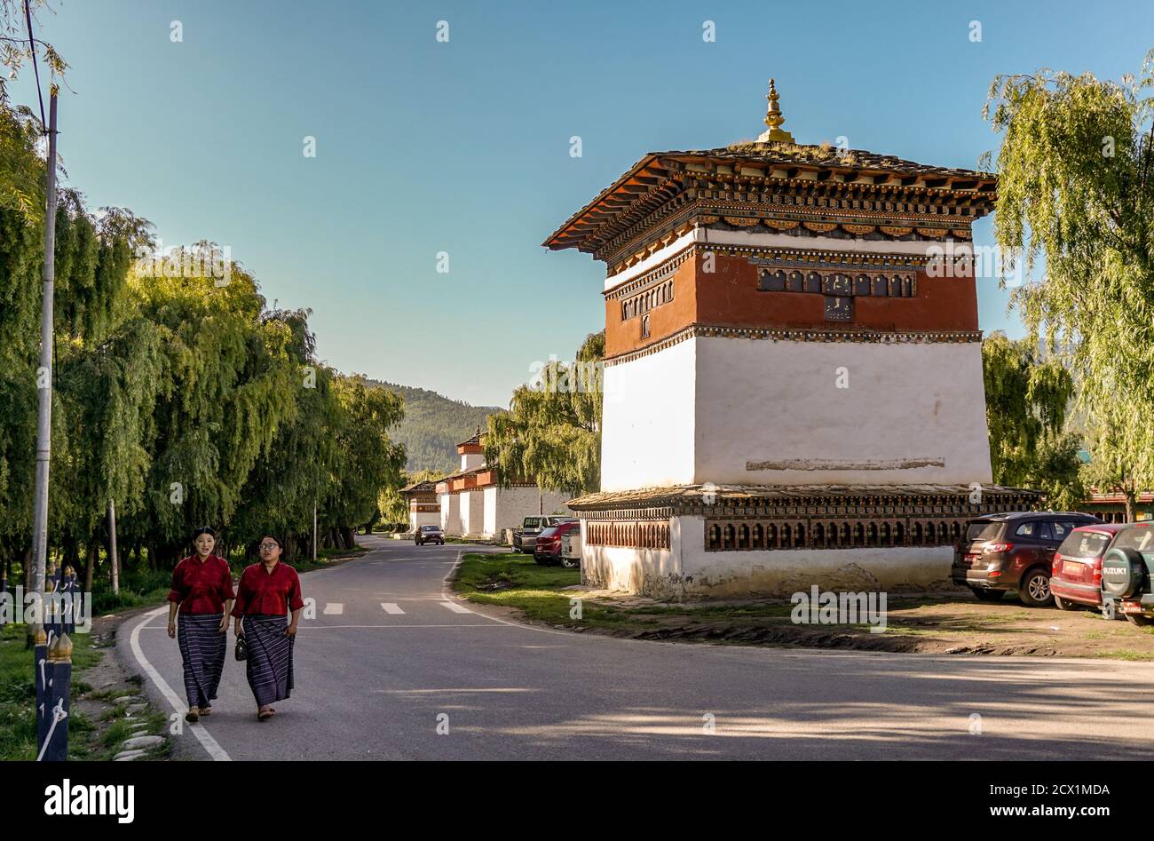 Two bhutanese girls in kira dress uniform walking by the Five chortens ...