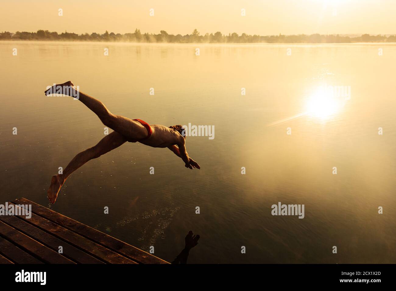 Active young man jumping into water from wooden pier Stock Photo - Alamy