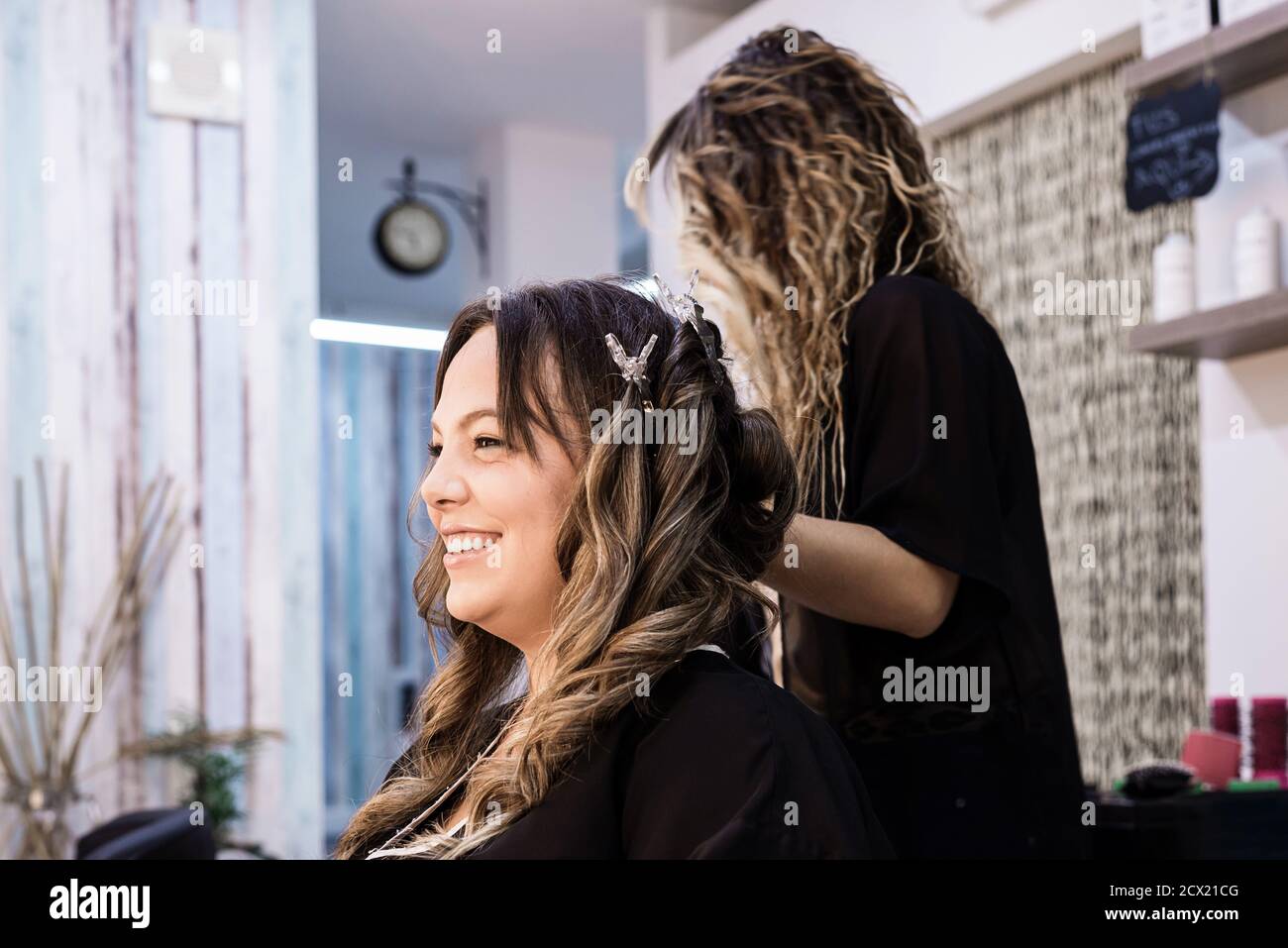 Hairdresser combing client with long curly hair against wall mirror at ...