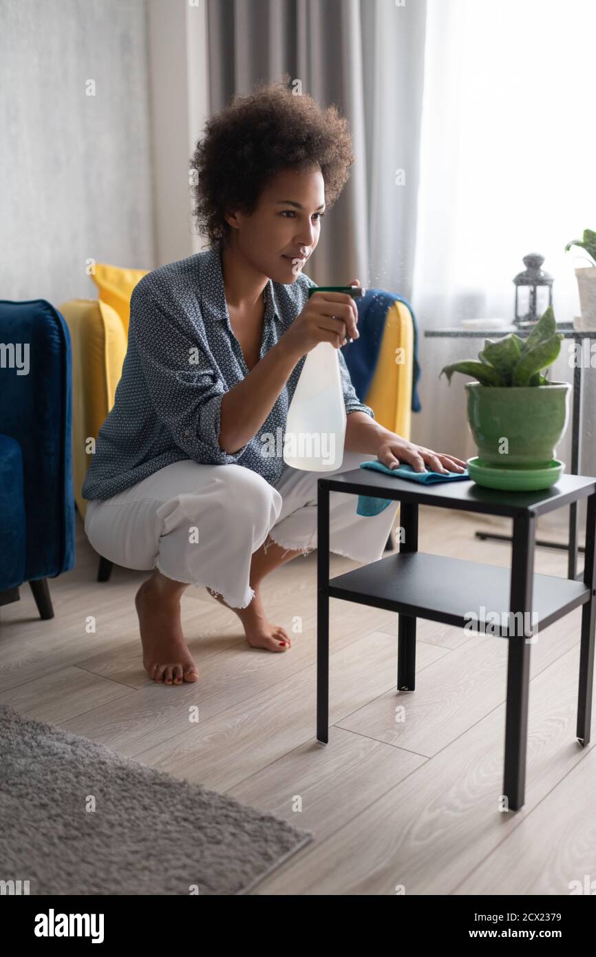 Full body black woman sitting on haunches and spraying green potted ...