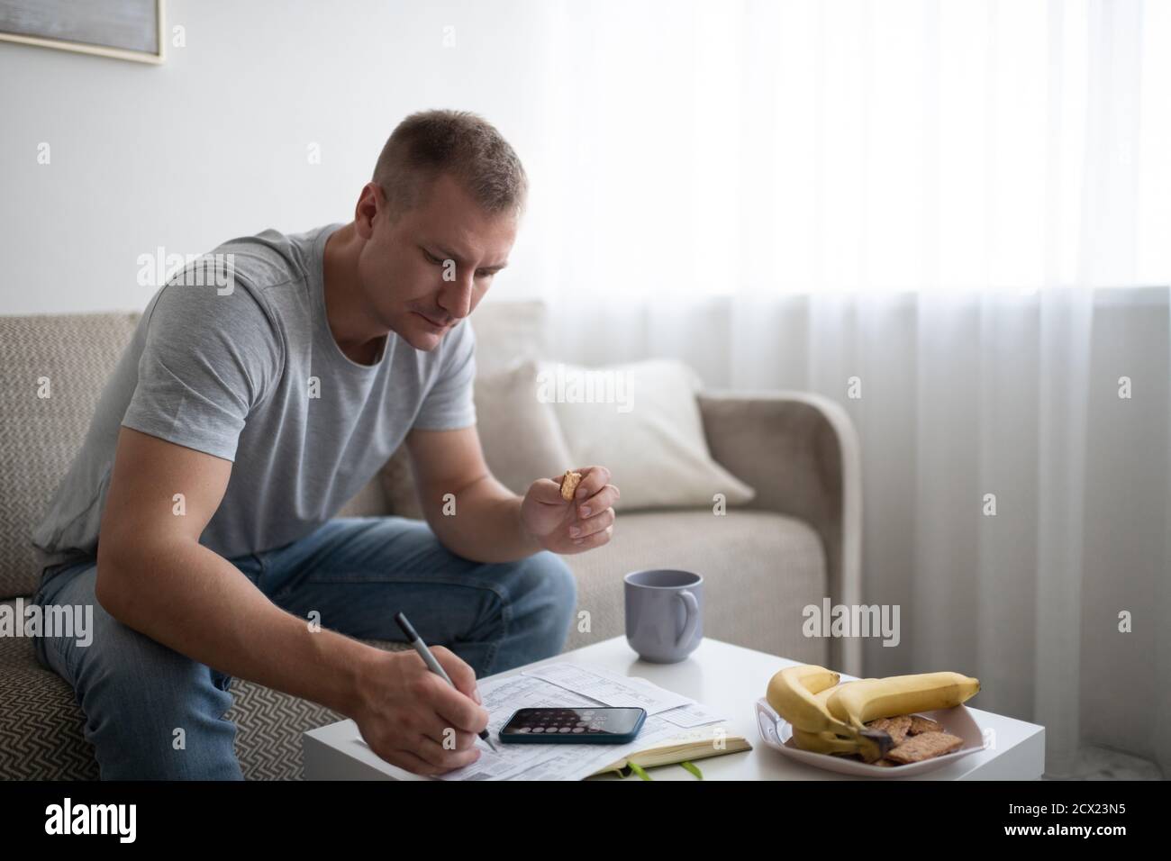 Adult male eating cookie and filling documents while managing personal ...