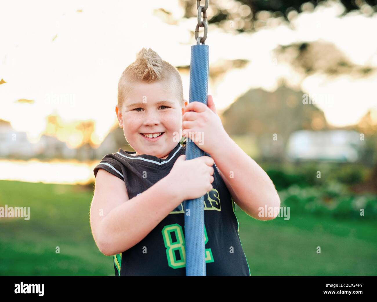 Young boy playing on swing at the park at sunset Stock Photo - Alamy