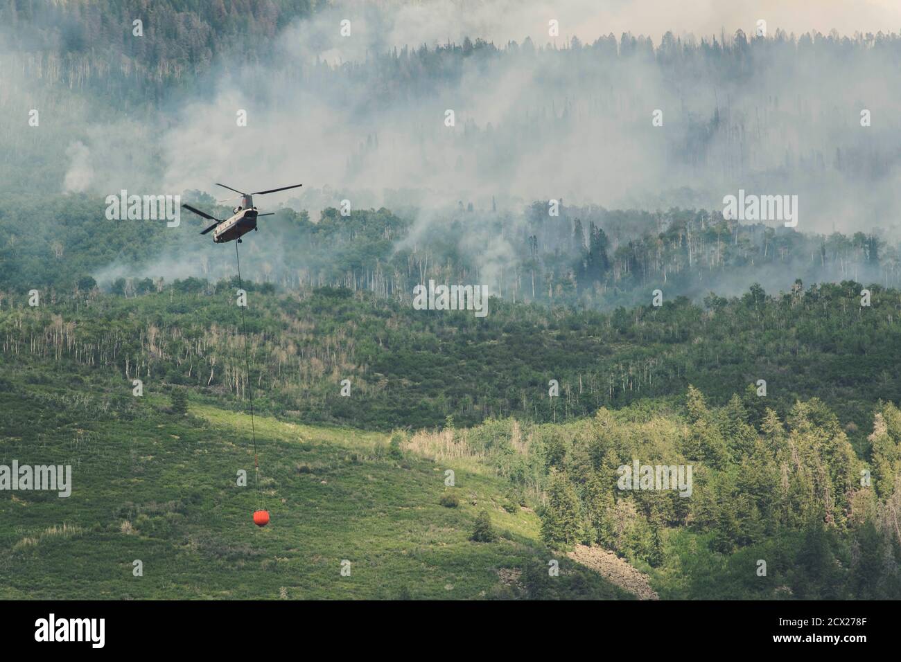 Helicopter flying with fire retardant while smoke emitting from ...