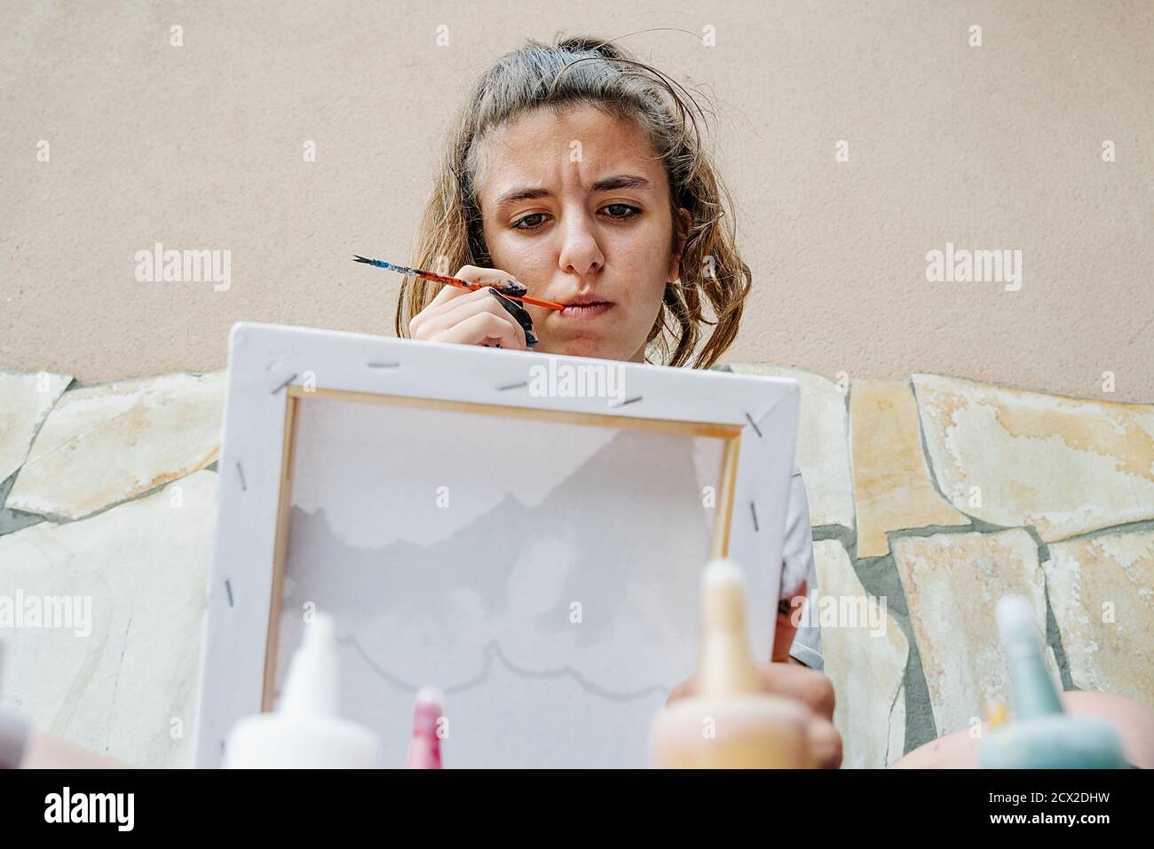 white girl biting a painting brush while thinking how continue her ...