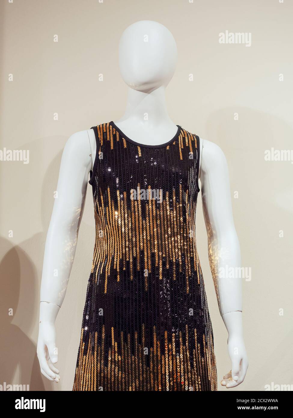 White faceless mannequin in a dress with black and gold sequins on a ...