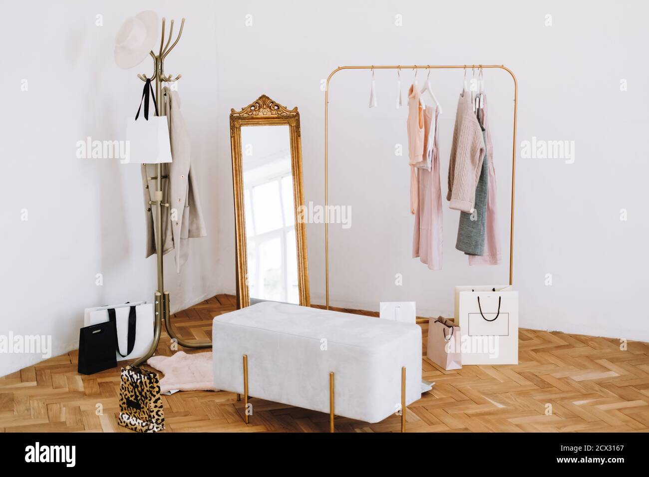 Rack with stylish women's clothes, grey pouf and mirror indoors ...