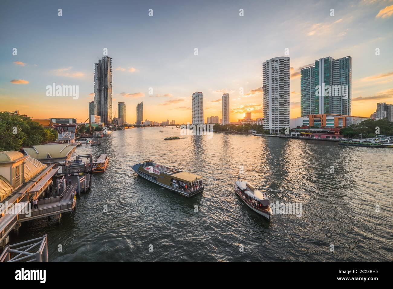 Chao Phraya River with Skyscrapers and Sathon Pier with Boats at Sunset ...