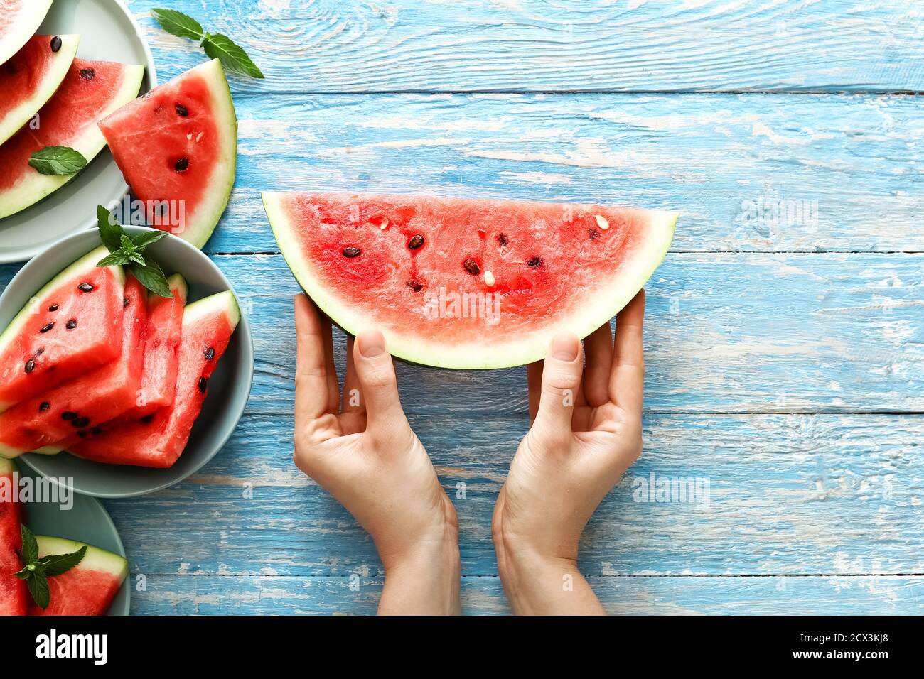 Fresh red watermelon slice in female hands on an blue rustic wood ...