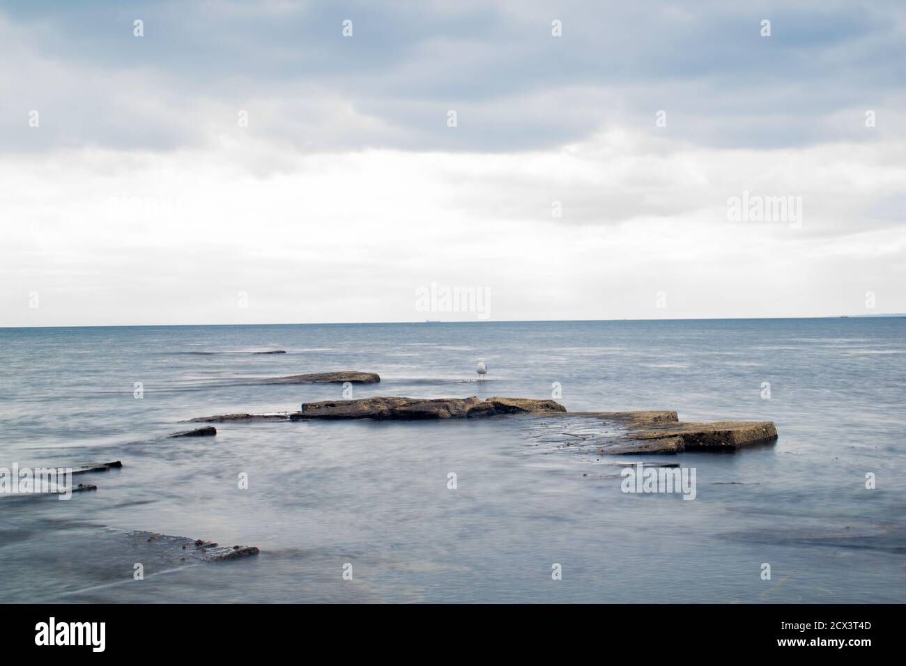 Long exposure shot of rocks sticking out of water and adramatic sky ...