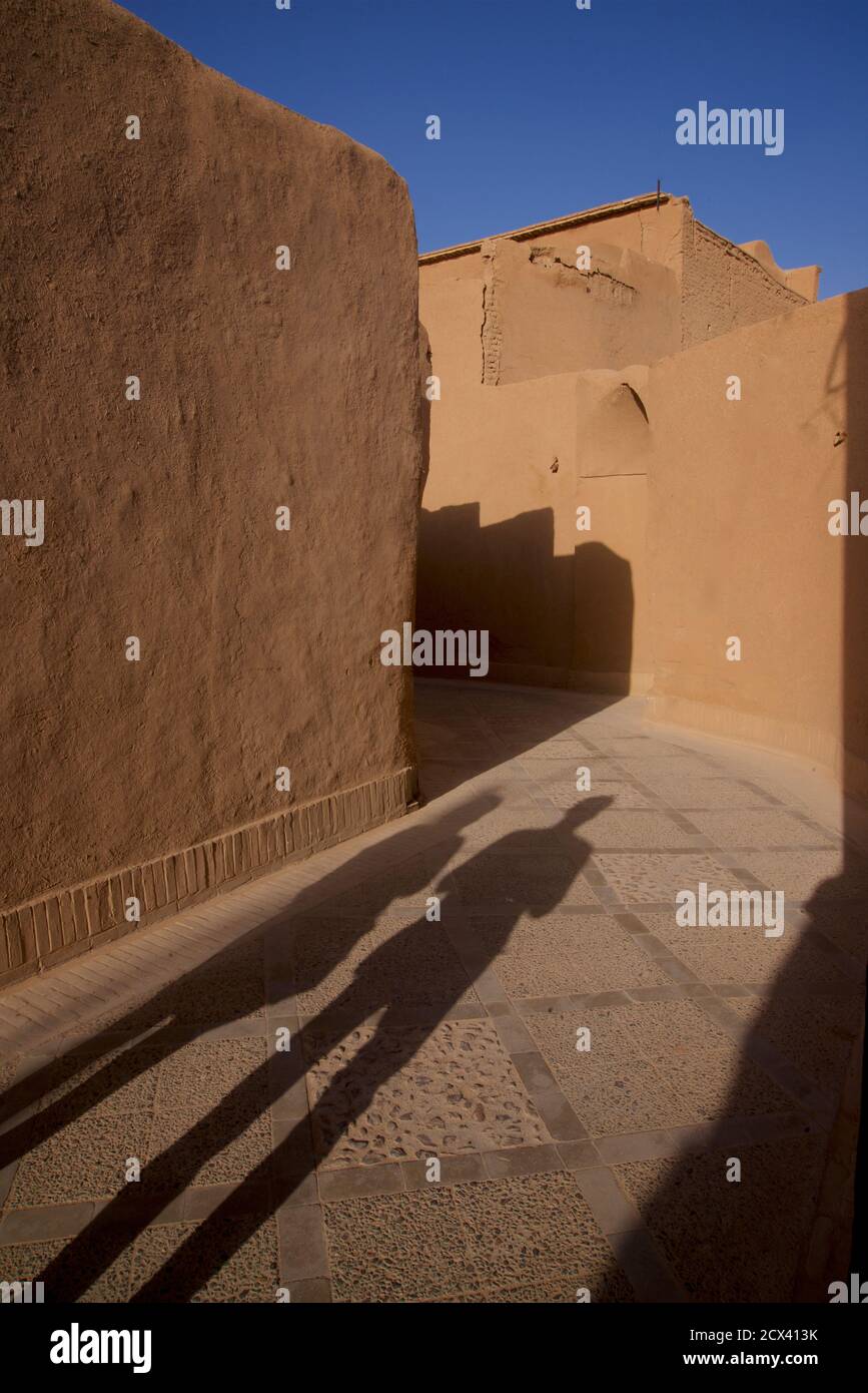 Long, late afternoon shadow of a tourist couple in the narrow, adobe ...