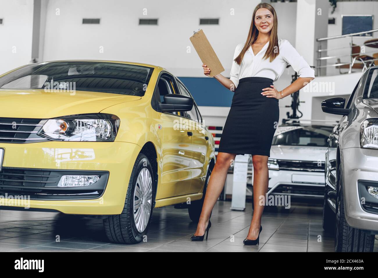 Attractive young female car dealer standing in showroom Stock Photo - Alamy