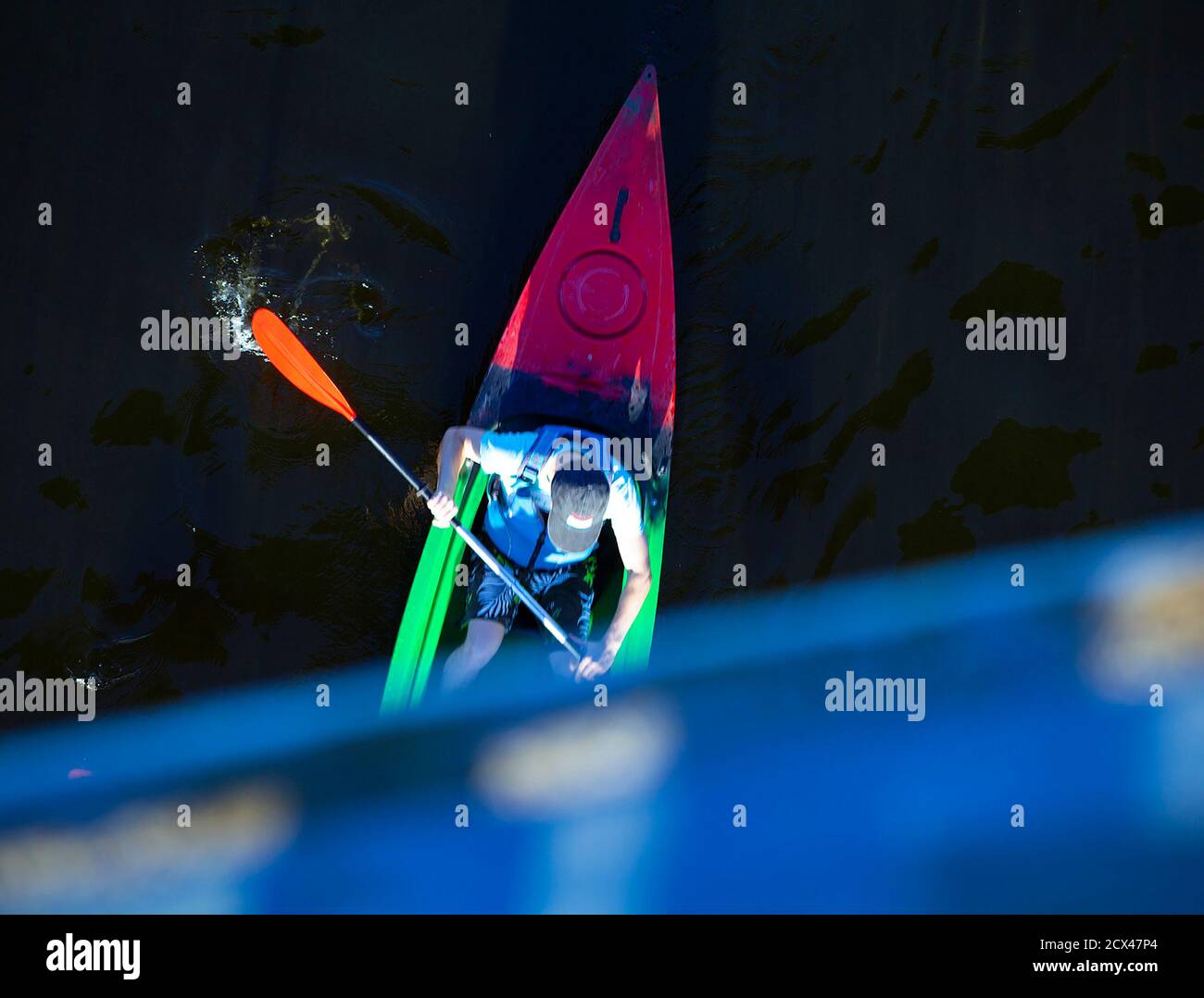 one person a man with an orange paddle in a bright red and green boat ...