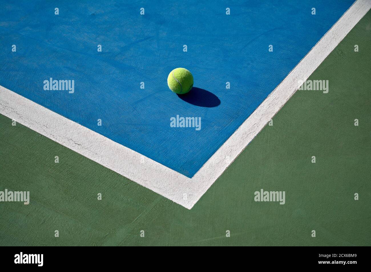 detail of a yellow tennis ball on the corner of a blue court with white ...