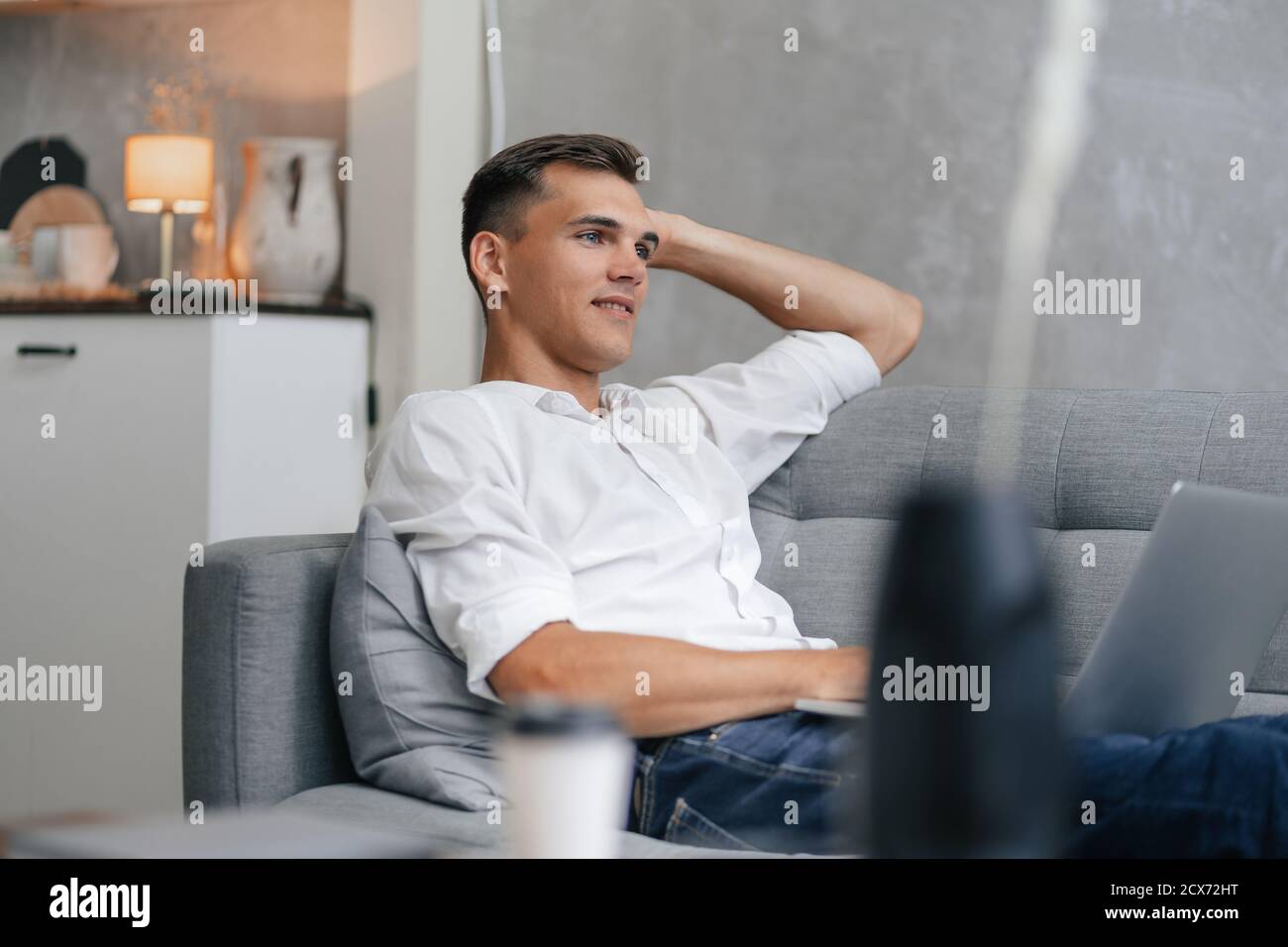 thoughtful young man with a laptop sitting on the couch Stock Photo - Alamy