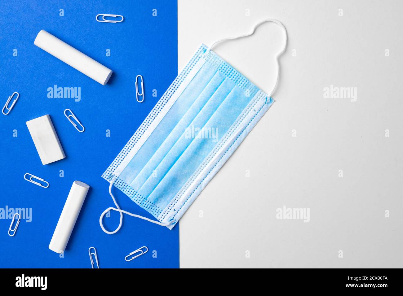 Pieces of chalk, paper clips and medical mask on blue and white ...