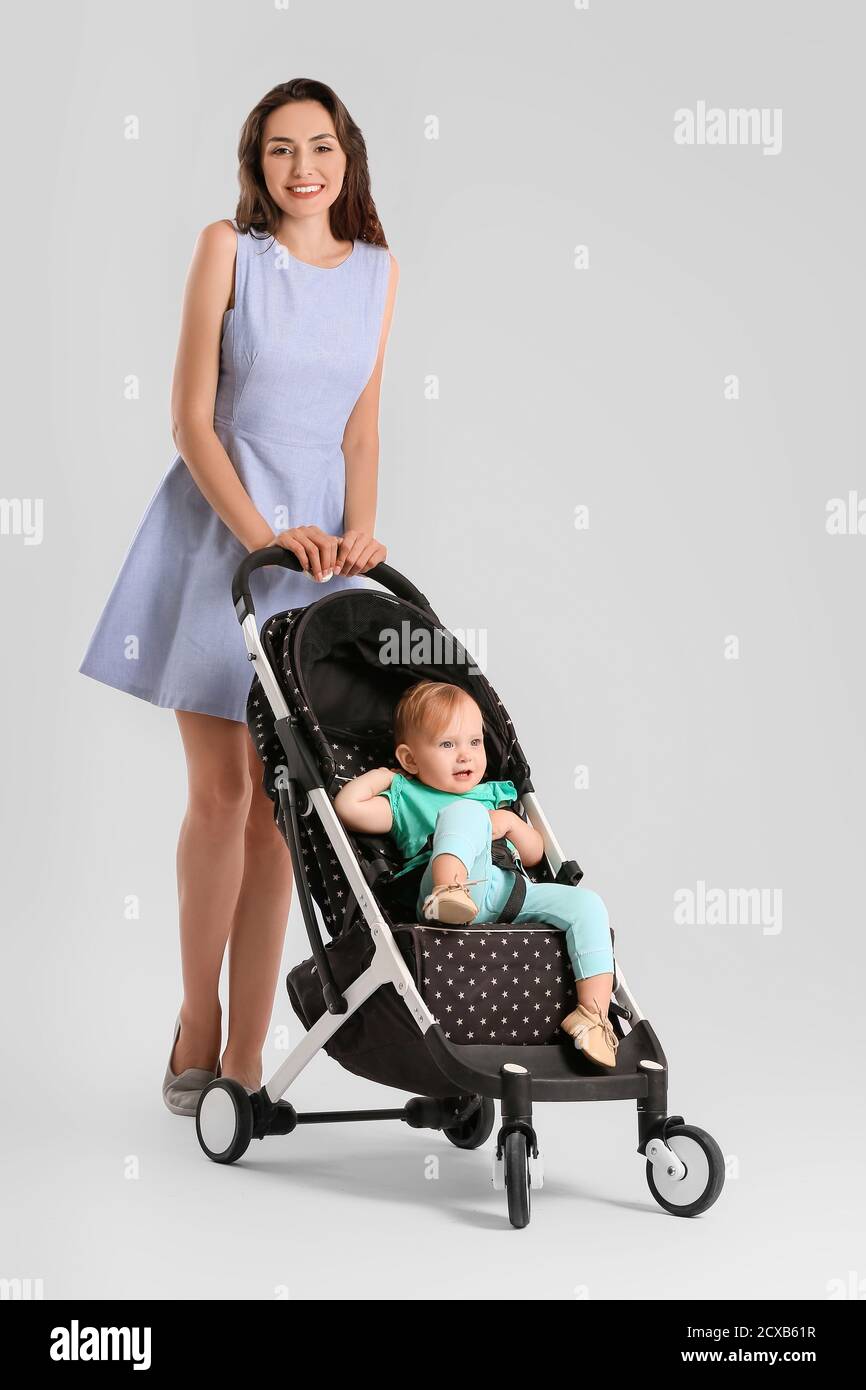 Woman and her cute baby in stroller on light background Stock Photo - Alamy