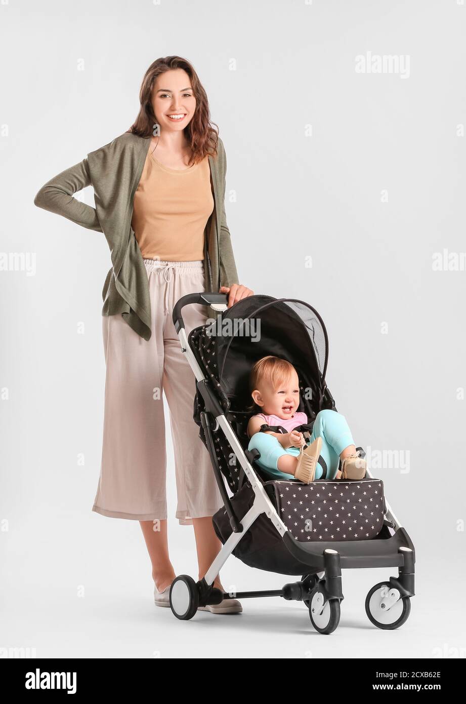 Woman and her cute baby in stroller on light background Stock Photo - Alamy