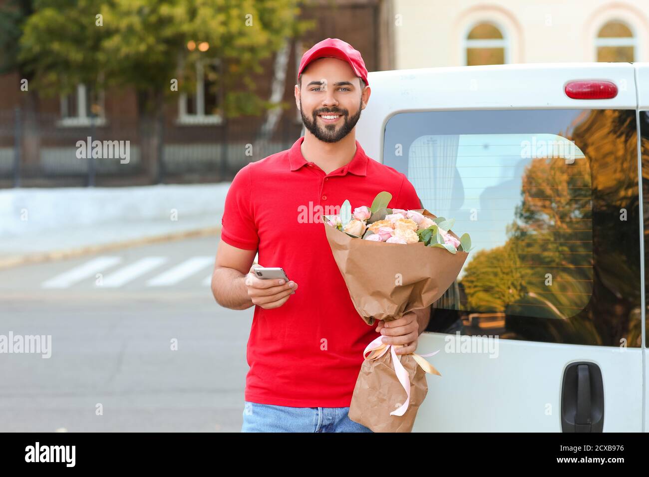 Delivery man with bouquet of beautiful flowers and mobile phone near ...