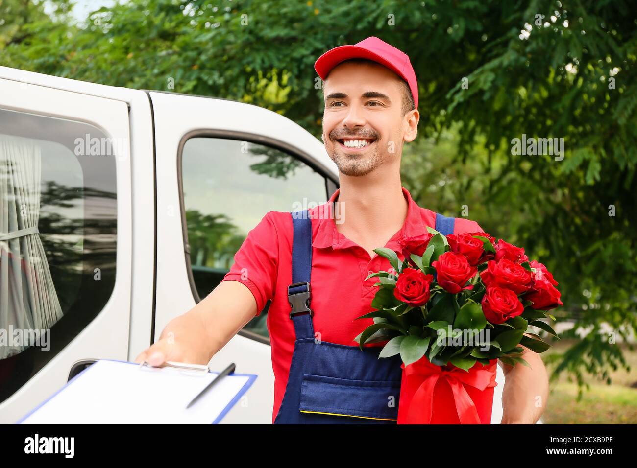 Delivery man with beautiful flowers and clipboard near car outdoors ...
