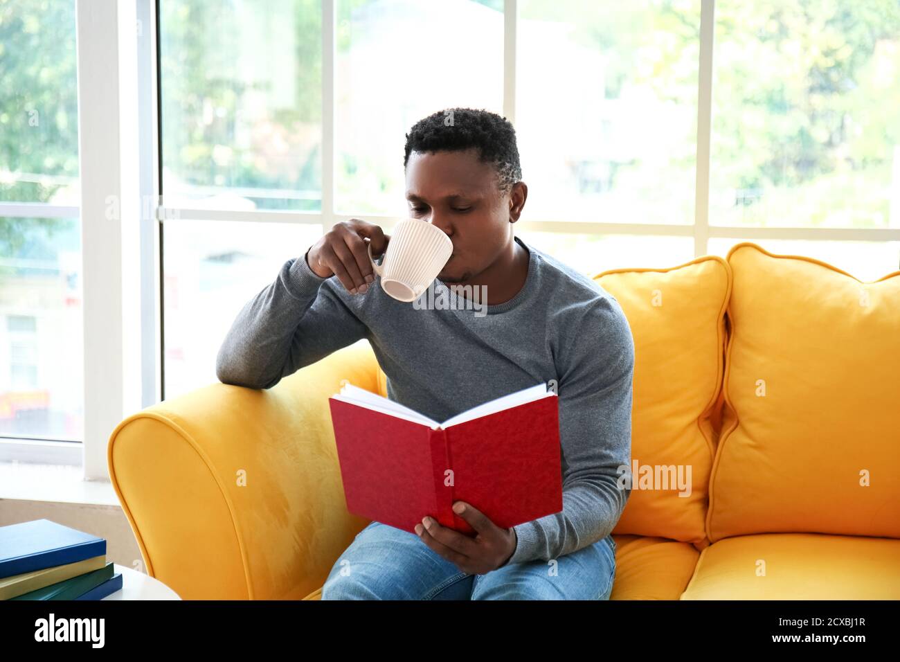 African-American man reading book and drinking coffee at home Stock ...