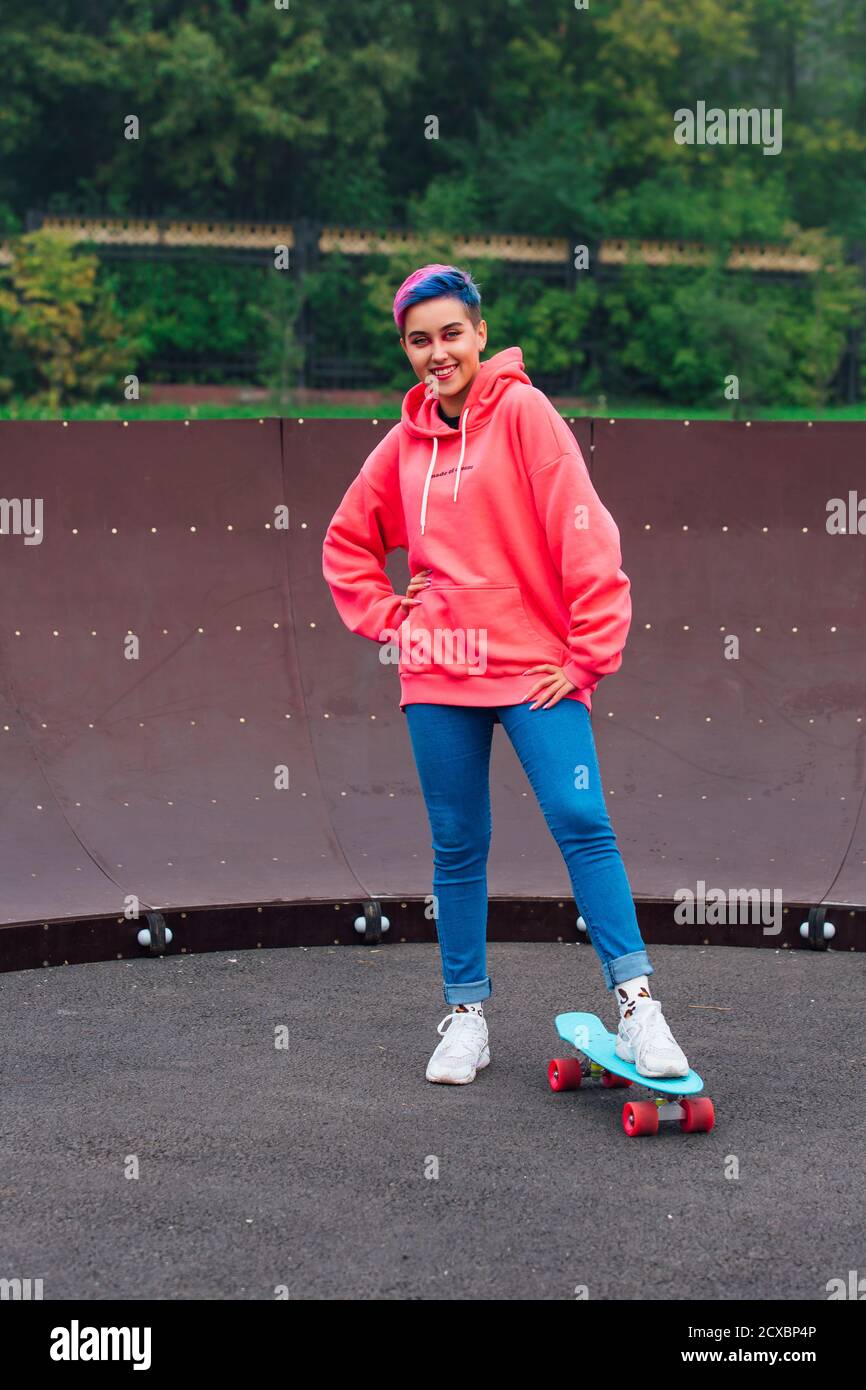 Portrait of a trendy pretty young girl standing next to the skateboard ...