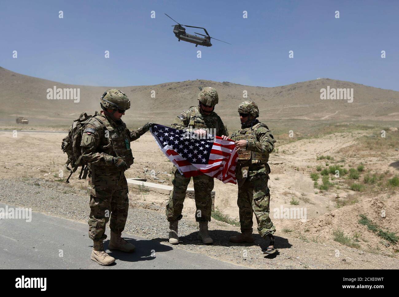 NATO soldiers stand with U.S. flag as a Chinook helicopter takes off ...