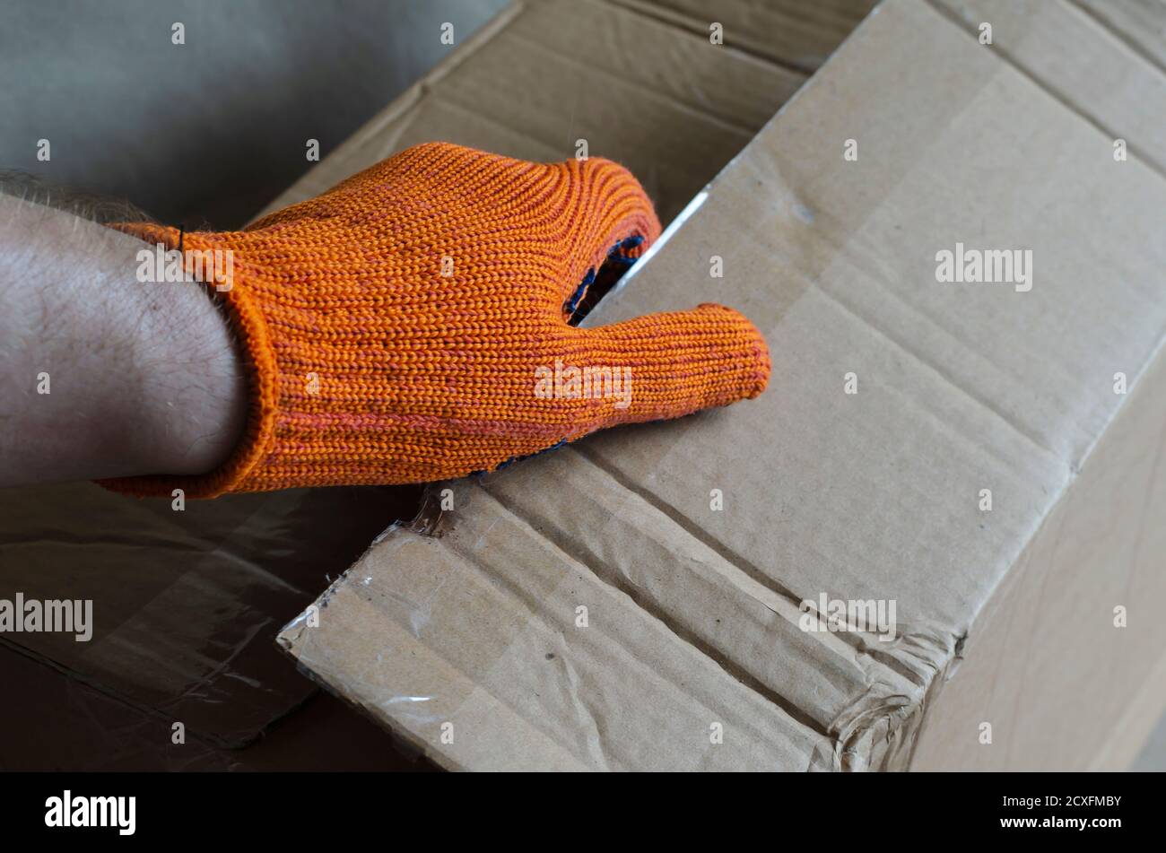 A worker wearing protective gloves opens a cardboard box. A hand with a ...