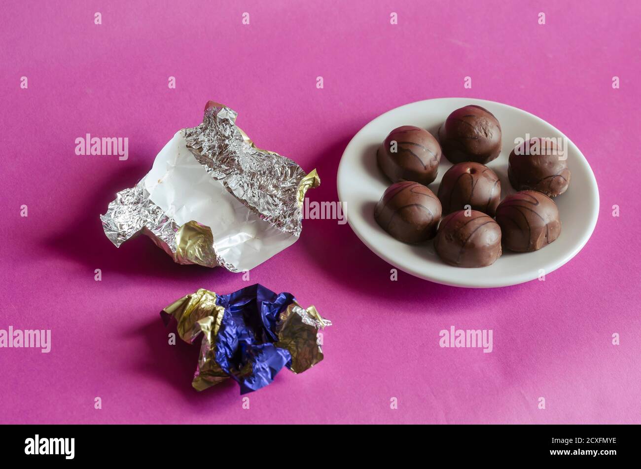 Chocolate candies in a white saucer on a pink background. A serving of ...