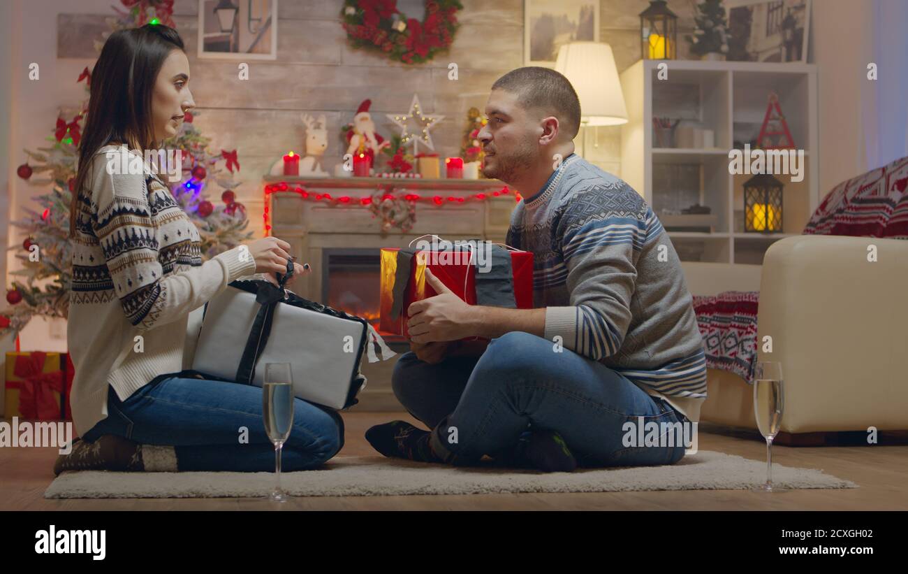 Cheerful couple giving each other gifts on christmas day in front of ...