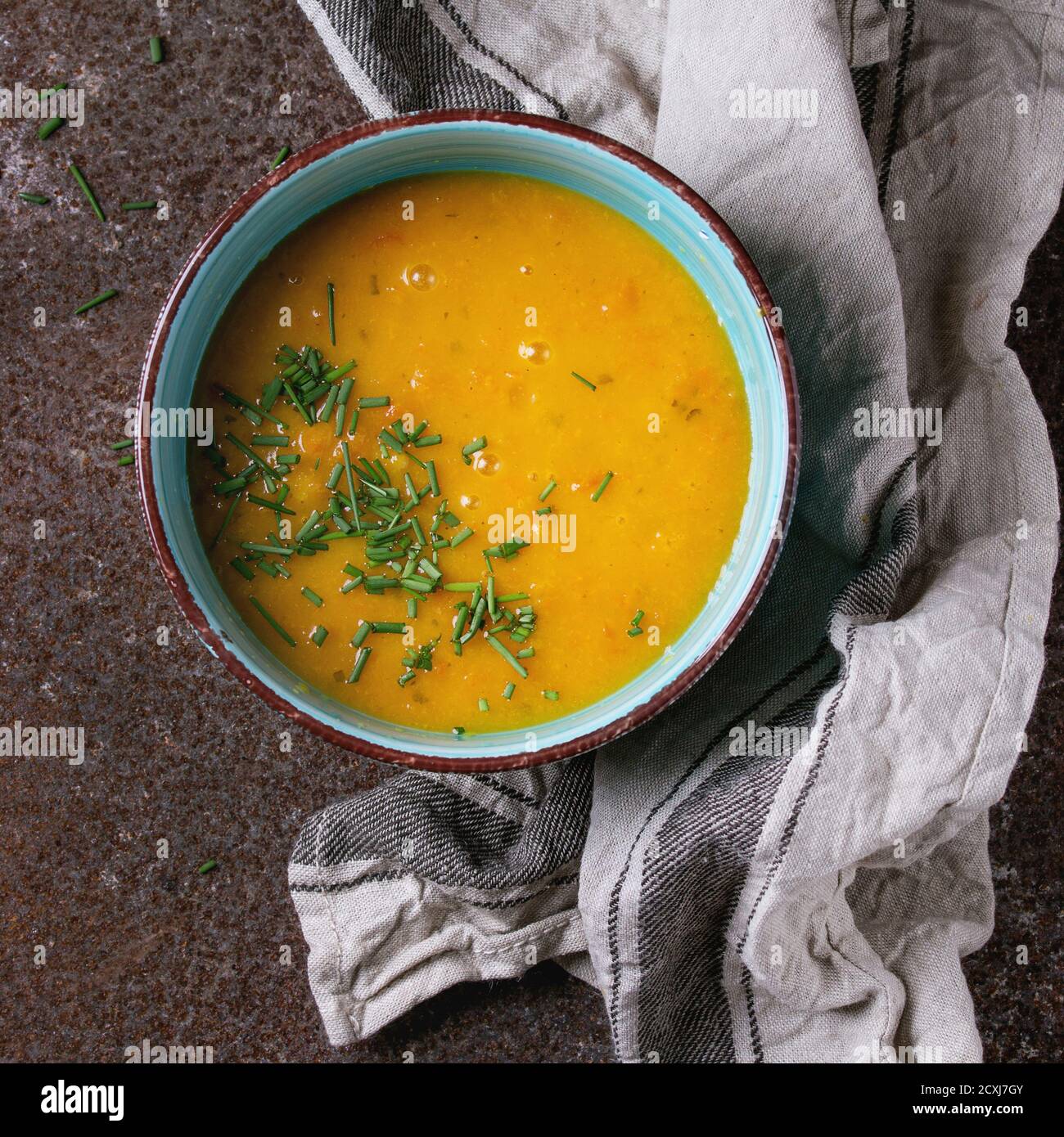 Blue ceramic bowl of carrot soup, served with onion chives and kitchen ...