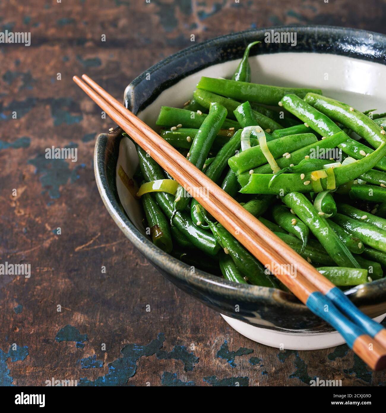Bowl of fried green beans with onion and sesame seeds, served with wood ...