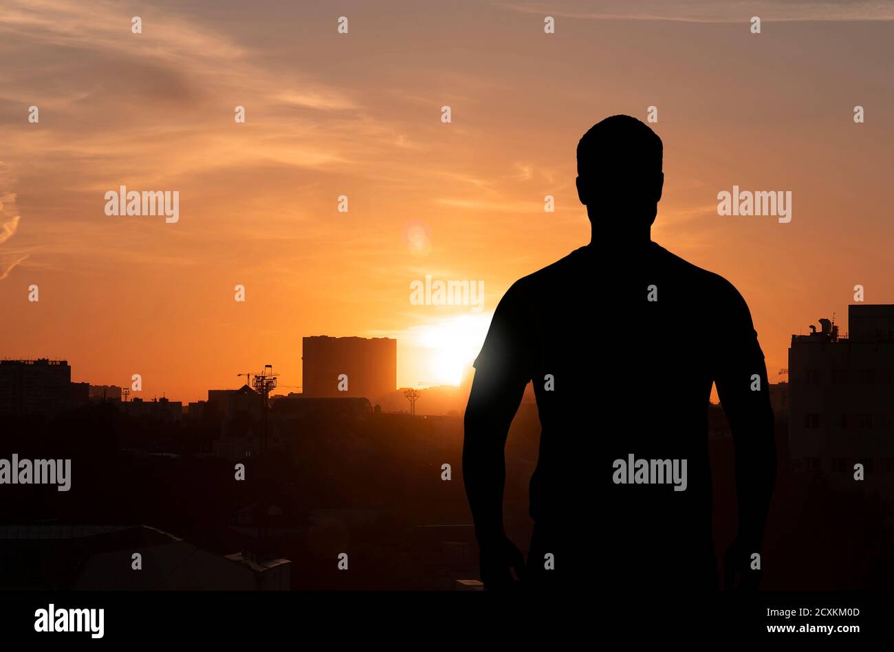 Silhouette of a man standing on top of building in front of city during ...
