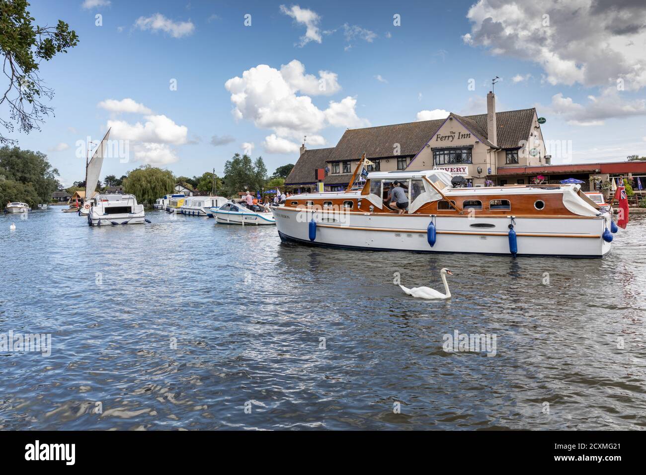 Boats travelling on the river Bure past the Ferry Inn Public House ...